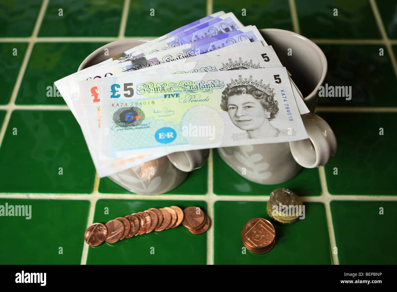 sterling notes on a mug and coins by the mug with green tiles as ...