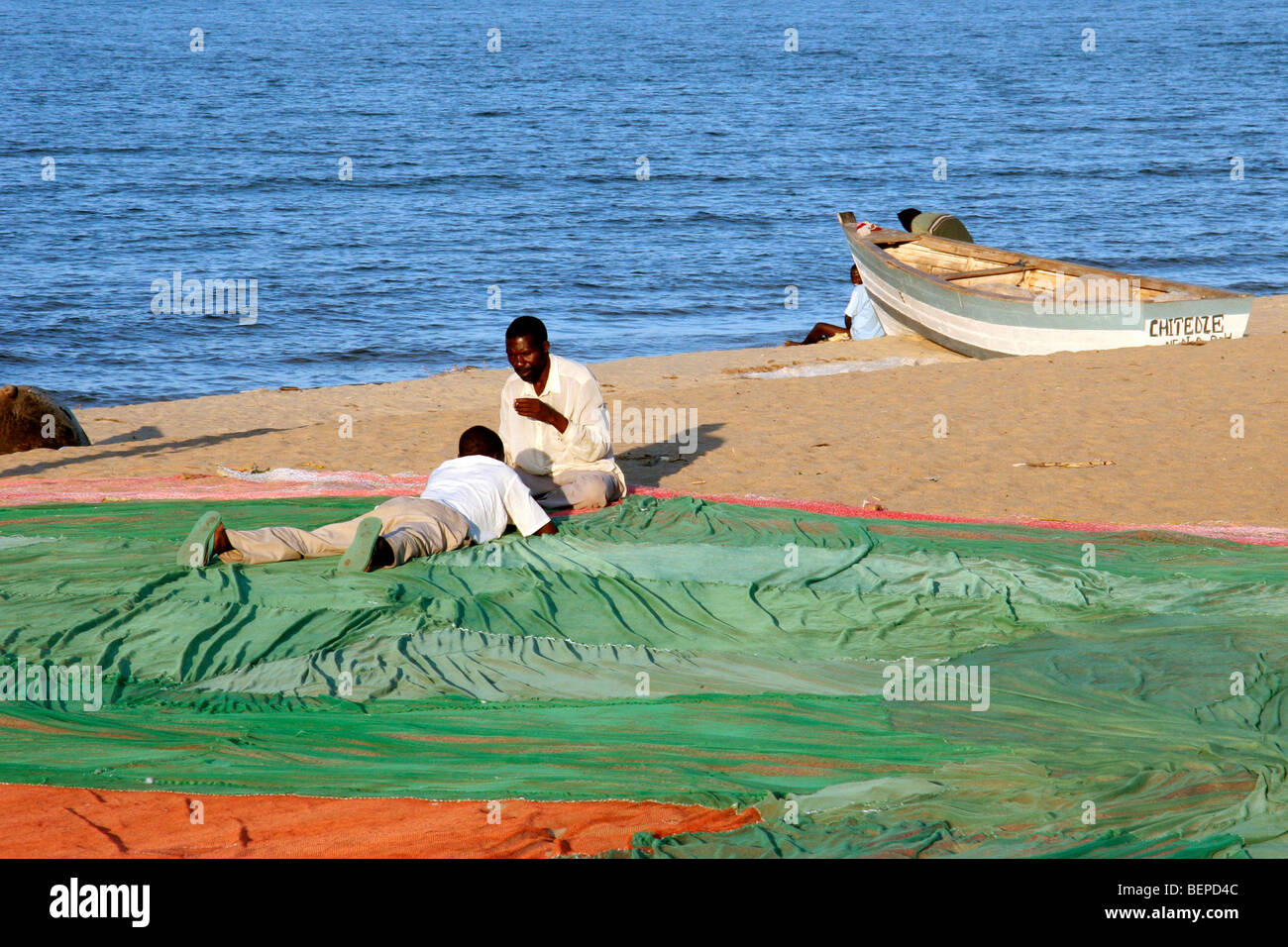 Two black fishermen mending sail of fishing boat on the beach along ...