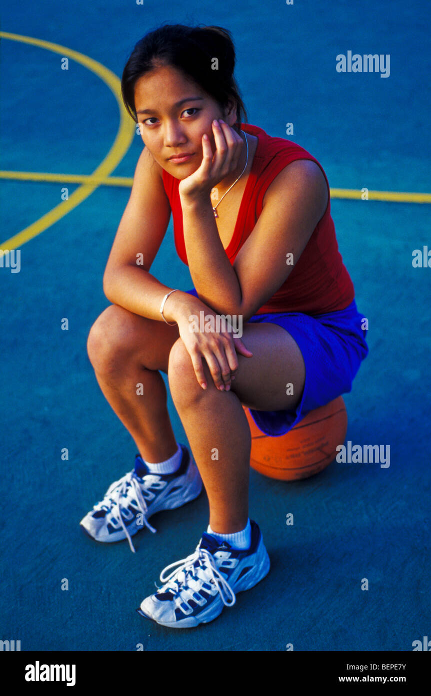 Teenage girl sitting on basketball on basketball court Stock Photo - Alamy
