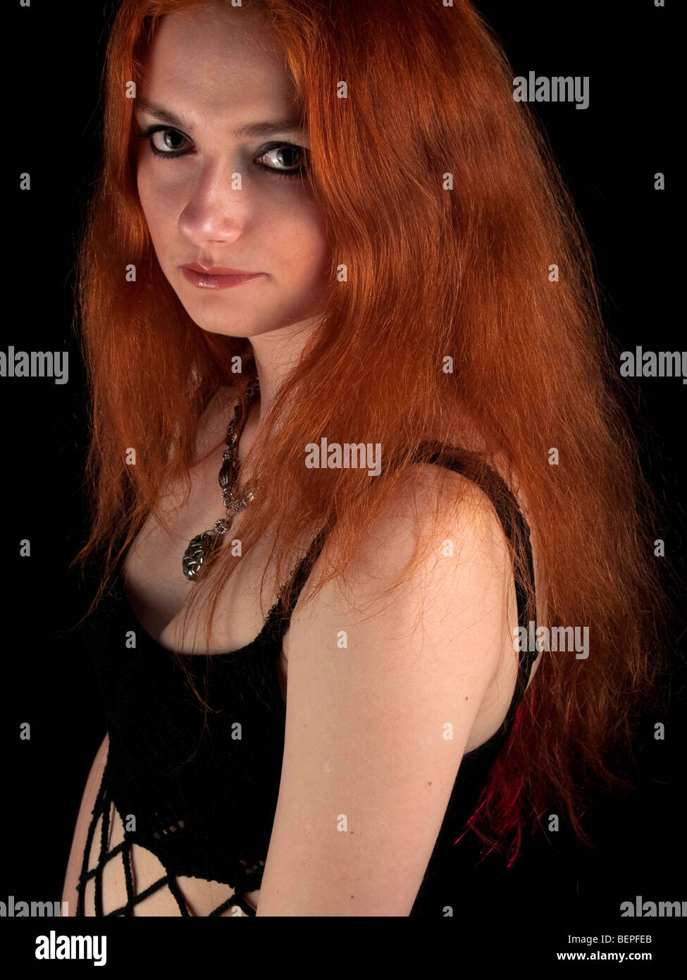 Beautiful red-haired young lady in evening dress on black background ...