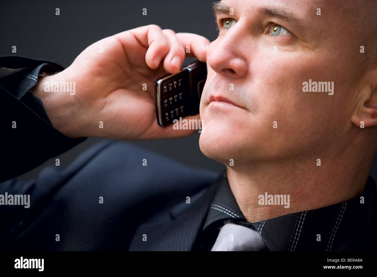 Bald man in his late 40's wearing a dark suit speaking on a cell phone ...