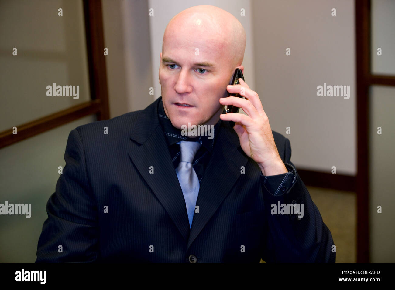 Bald man in his late 40's wearing a dark suit speaking on a cell phone ...