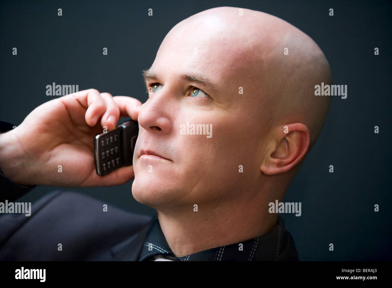 Bald man in his late 40's wearing a dark suit speaking on a cell phone ...
