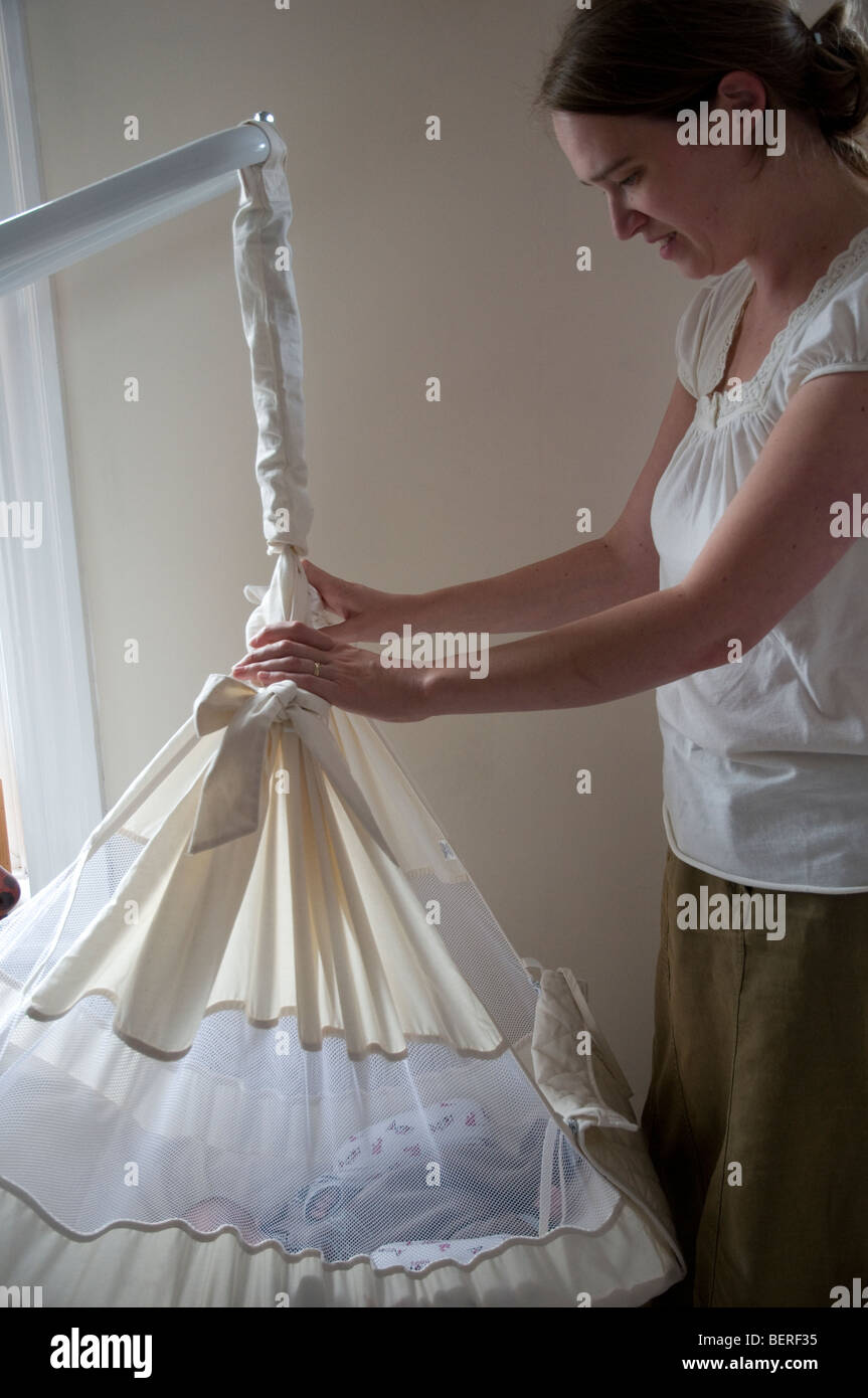 Mother looking at her newborn baby lying in a hanging cradle, 11 weeks ...
