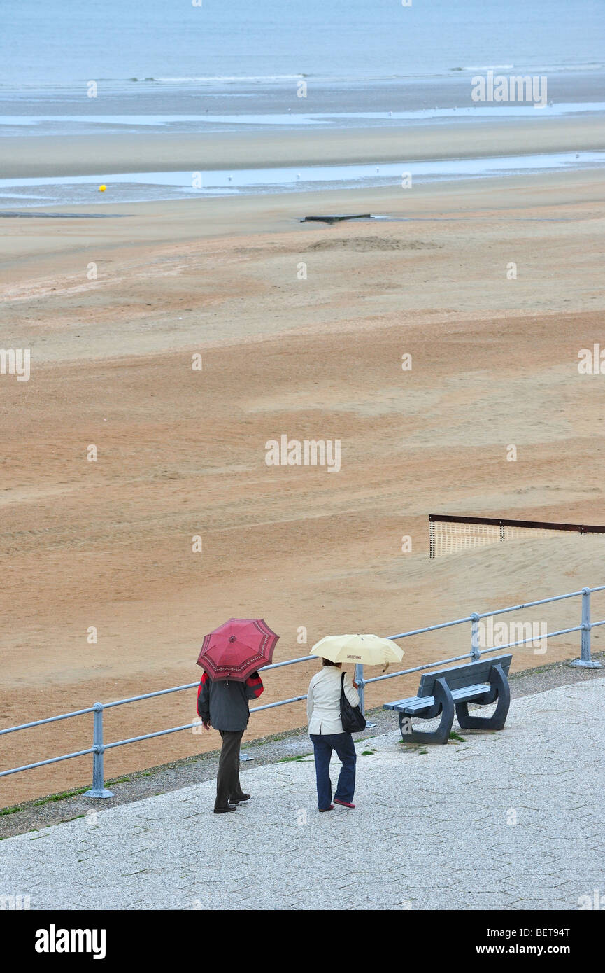 Tourists with umbrellas walking on promenade along North Sea beach at ...