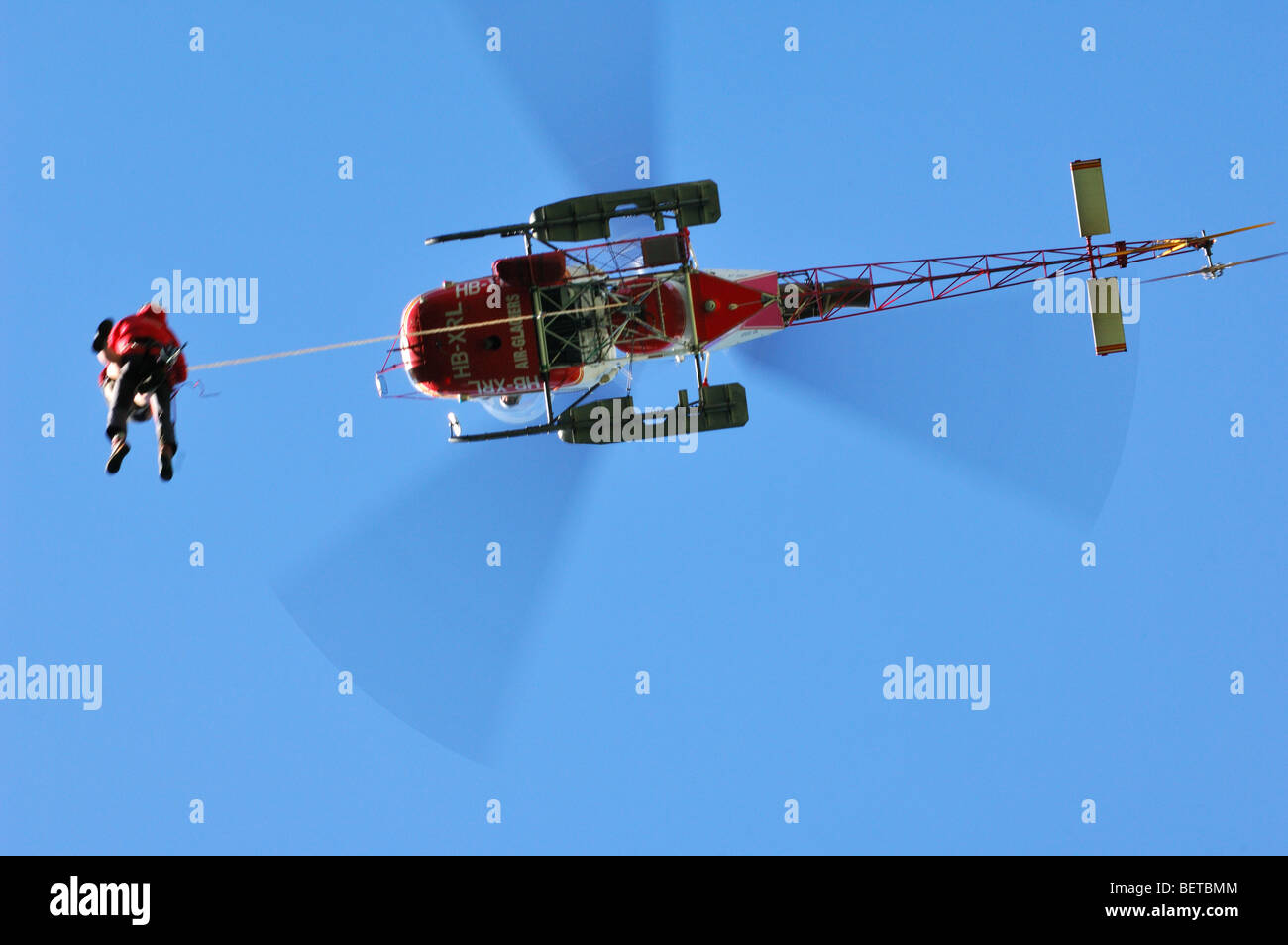 Swiss rescue helicopter in flight winching rescuer and climber / victim ...