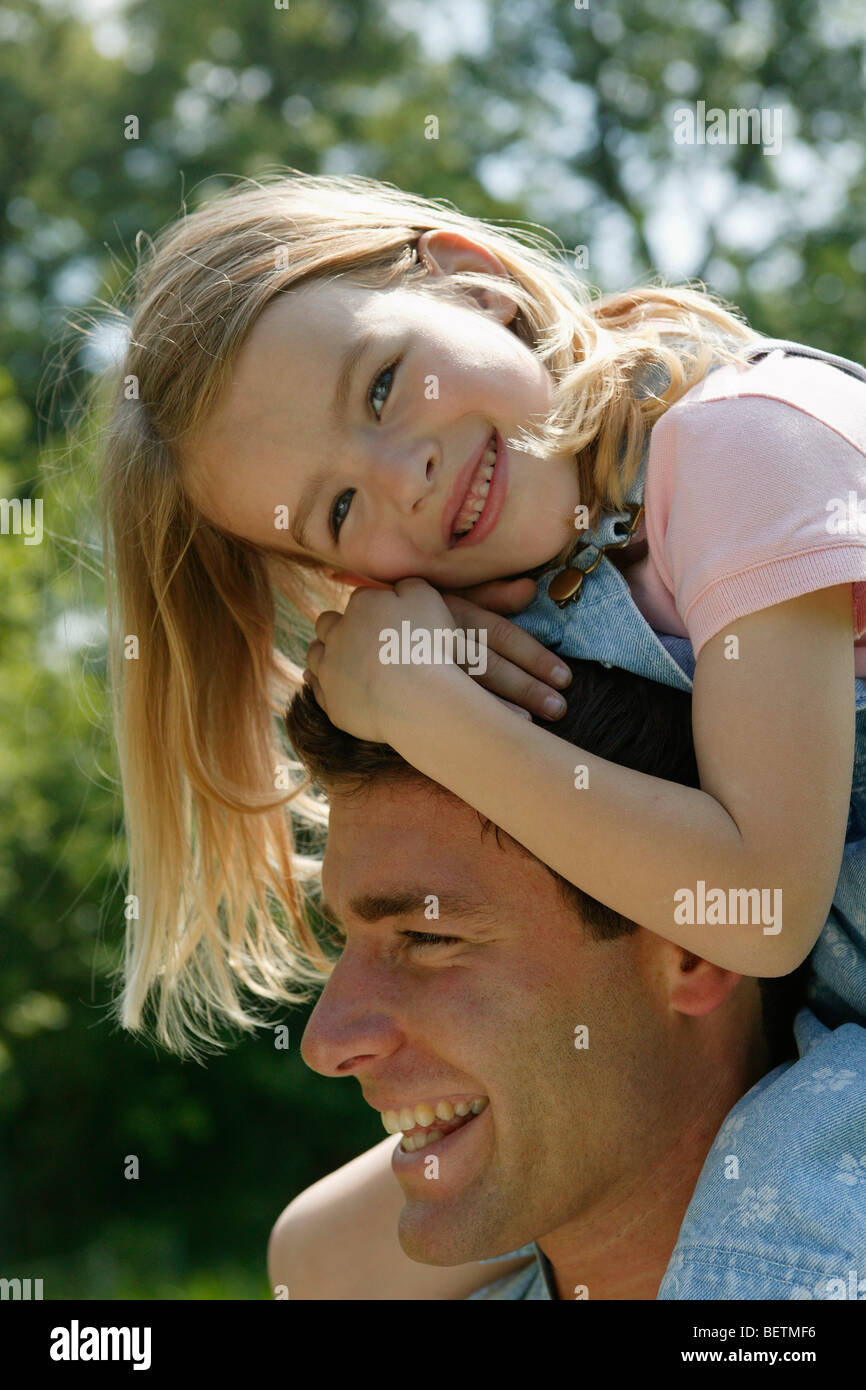 happy young girl sitting on her fathers shoulders leaning against his ...
