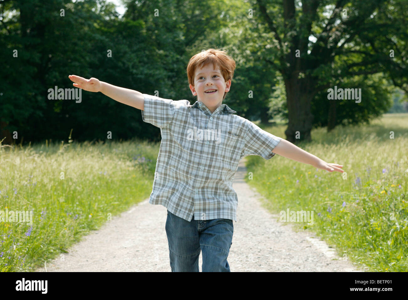 young boy on a path in the park with arms outstretched like a plane ...