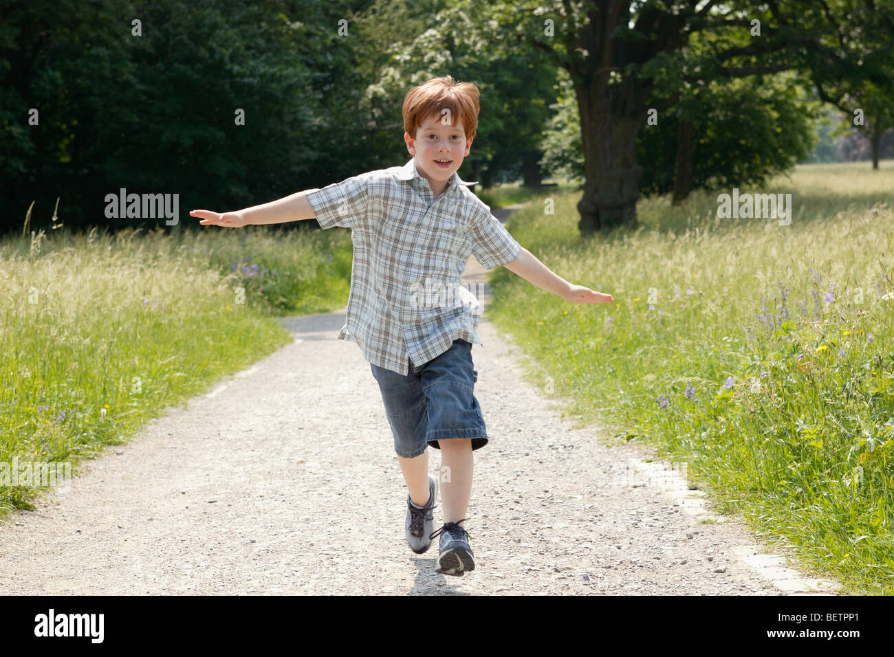 young boy running on a path in the park holding out his arms like an ...