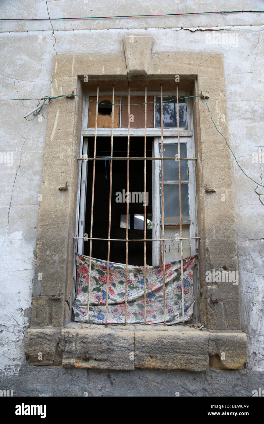 old barred open wooden window covered with a cloth in a run down area ...