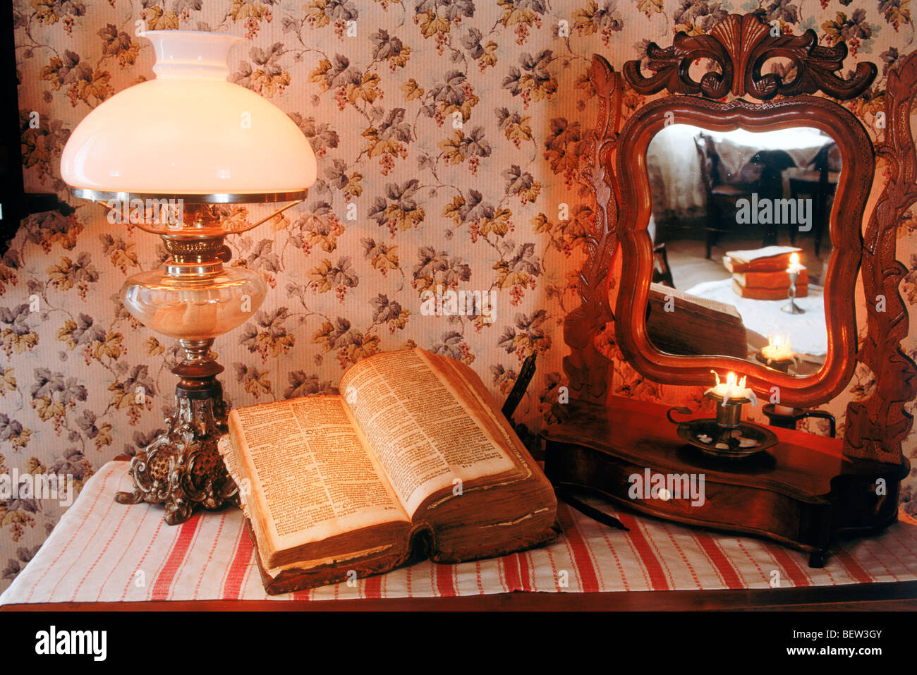 Antique wooden bureau with Bible, lamplight and mirror reflecting ...