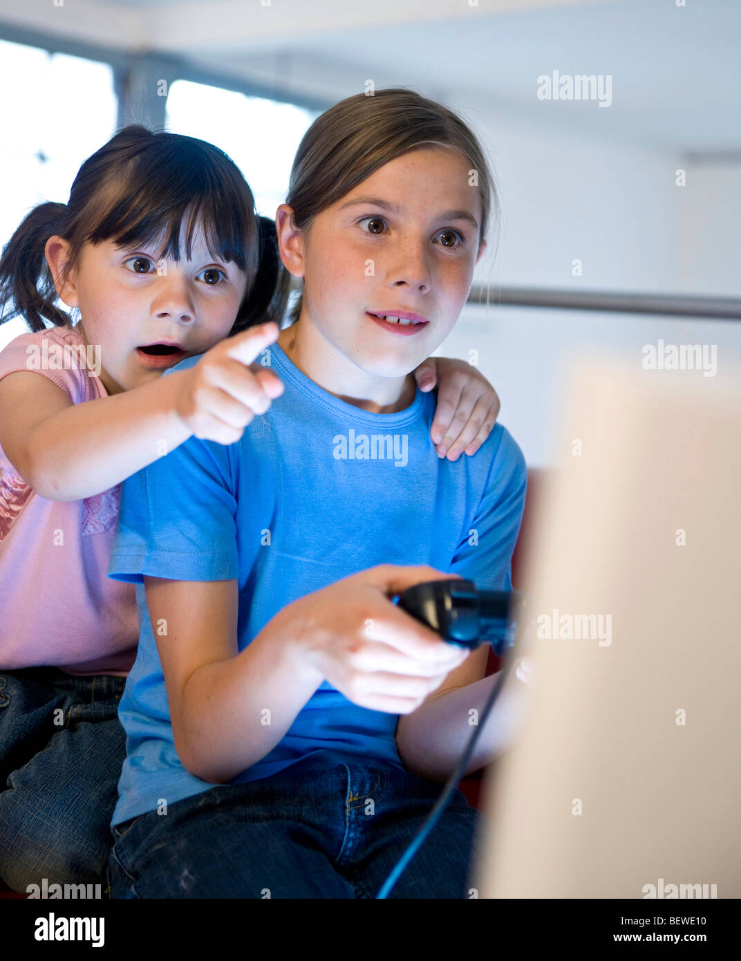 Girl playing a computer game while her sister is pointing at the screen ...