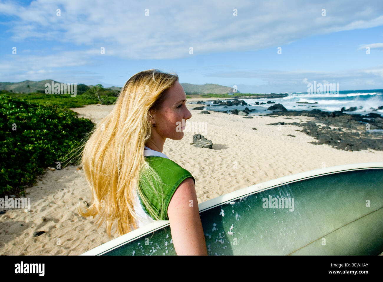 Side profile of a young woman carrying a surfboard on the beach, Hawaii ...