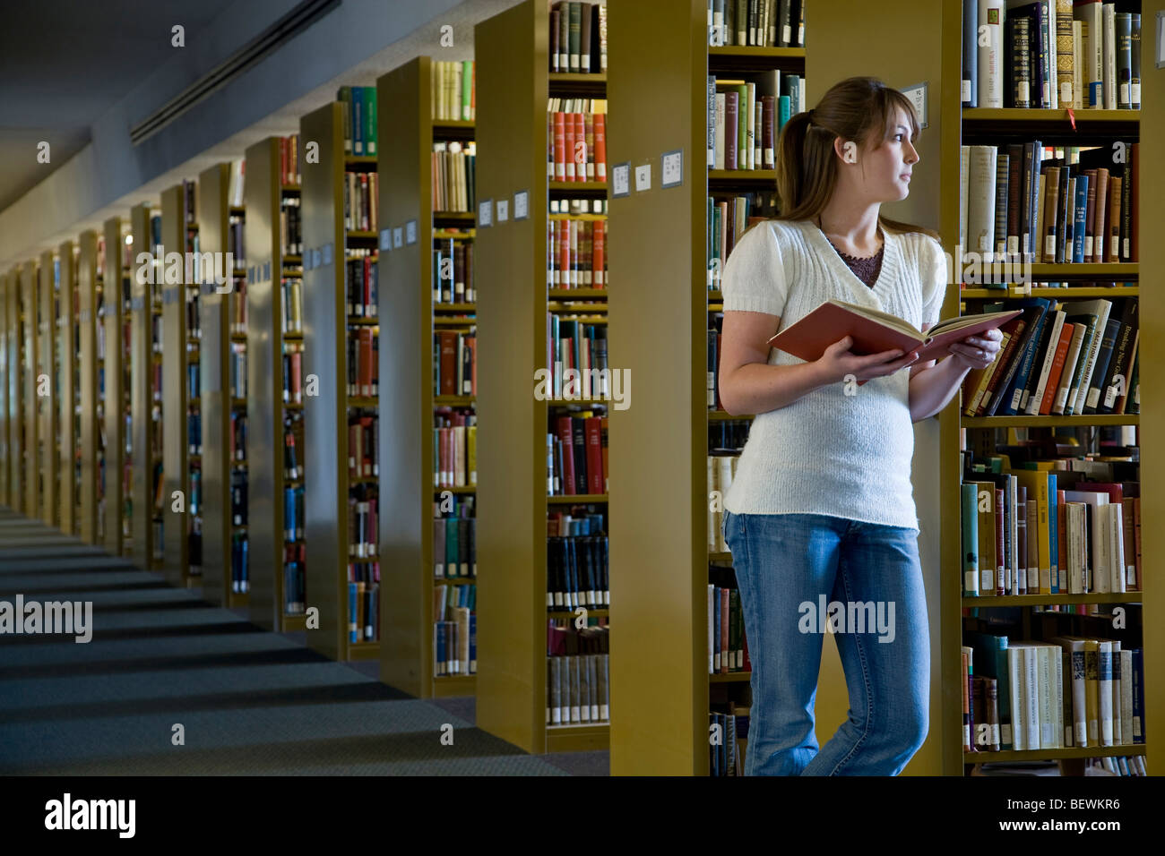 Woman reading a book by the stacks in a library Stock Photo - Alamy