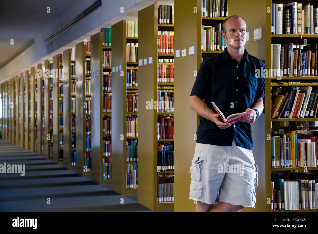 Man reading a book by the stacks in a library Stock Photo - Alamy