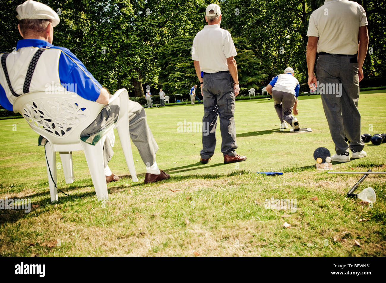 A Lawn Bowls player sitting in a plastic chair watches a bowling ...
