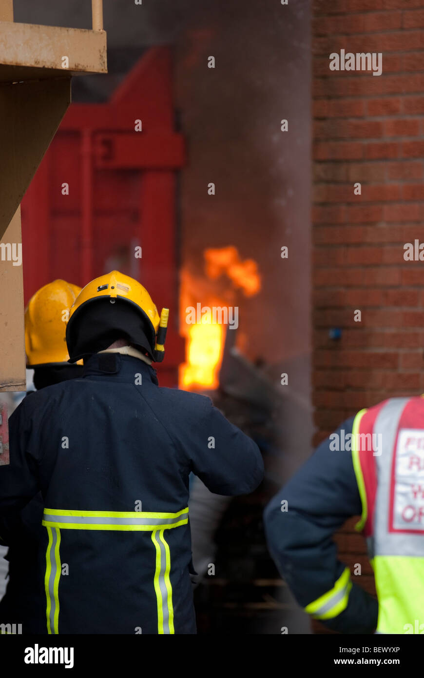 Firefighters entering factory on fire with flames in background Stock ...