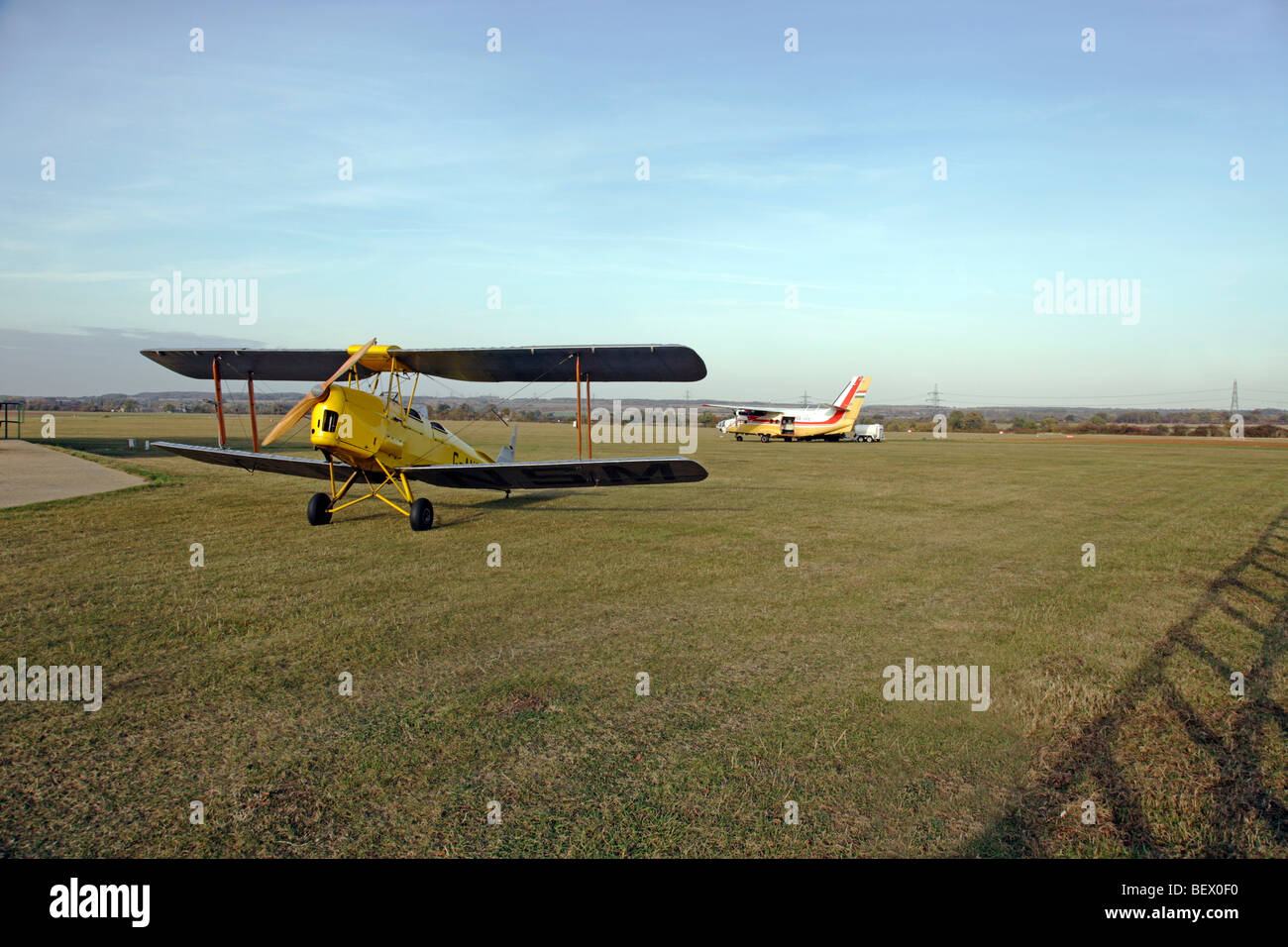 A bright yellow Tiger Moth bi-plane and pilot on an old airfield at ...