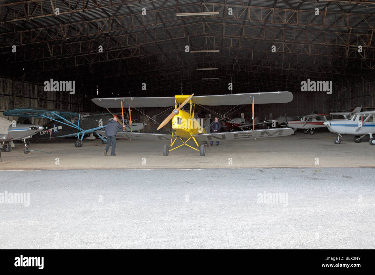 A bright yellow Tiger Moth bi-plane and pilot on an old airfield at ...