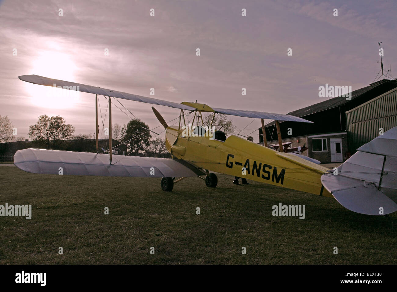 A bright yellow Tiger Moth bi-plane and pilot on an old airfield at ...