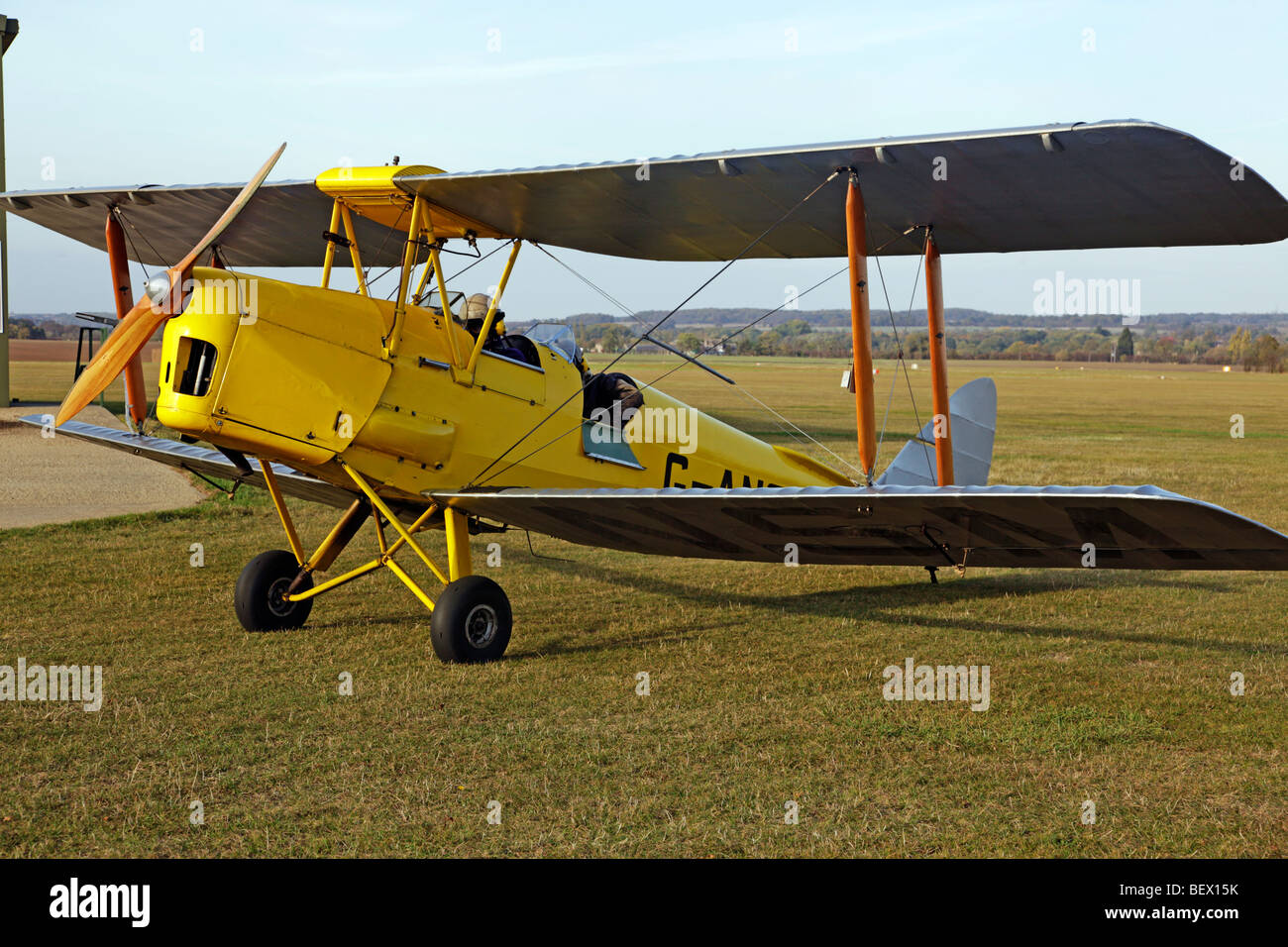 A bright yellow Tiger Moth bi-plane and pilot on an old airfield at ...