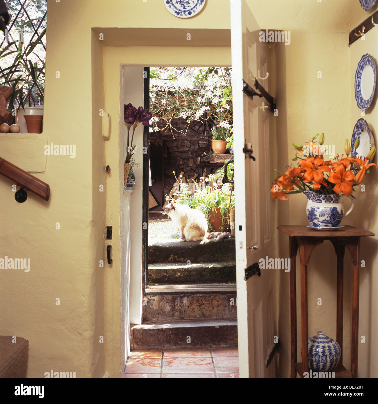 Cream cottage hall with jug of orange lilies on table beside open front ...