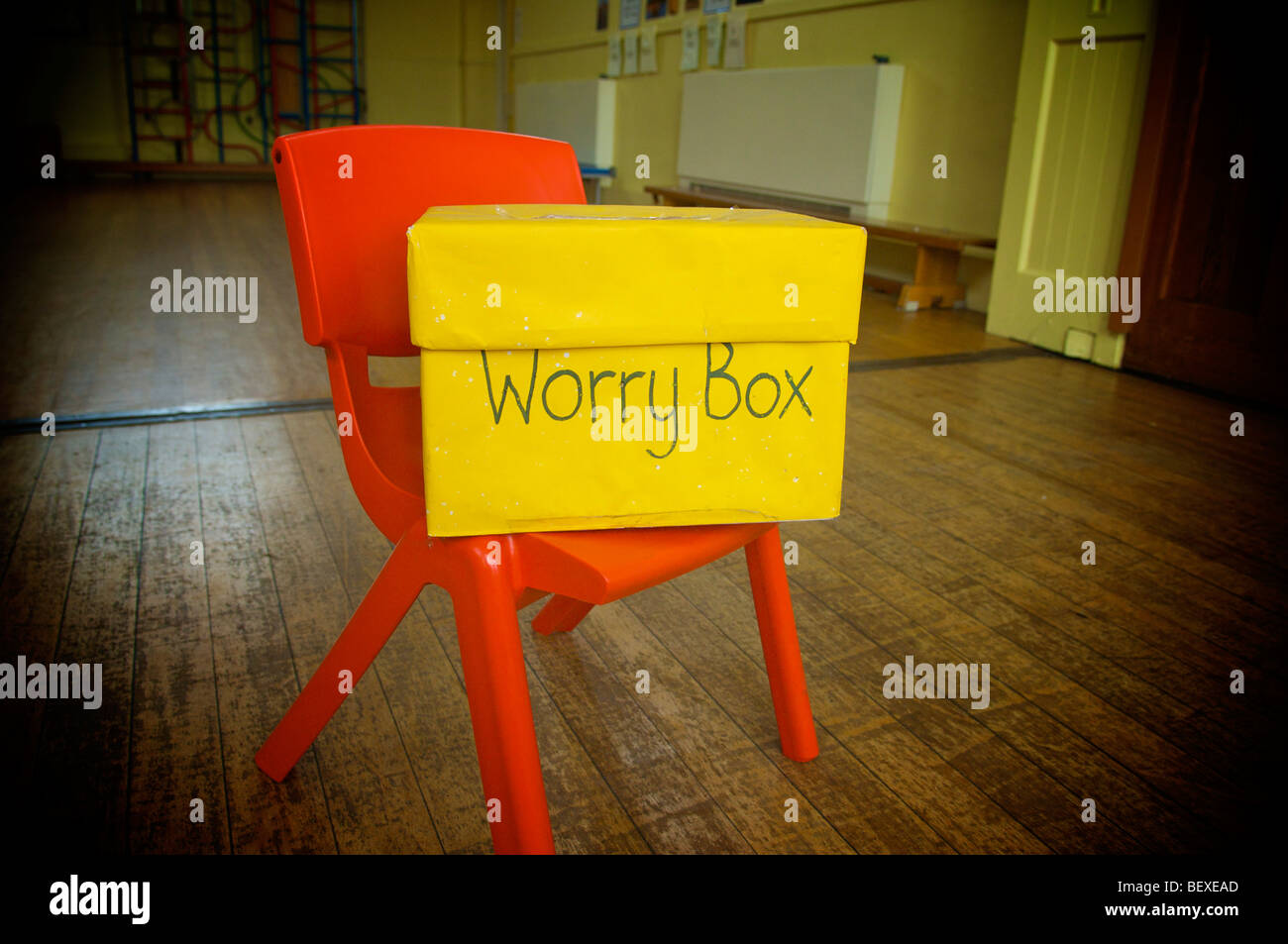 Bright yellow worry box on red chair sat in school hall for children to ...