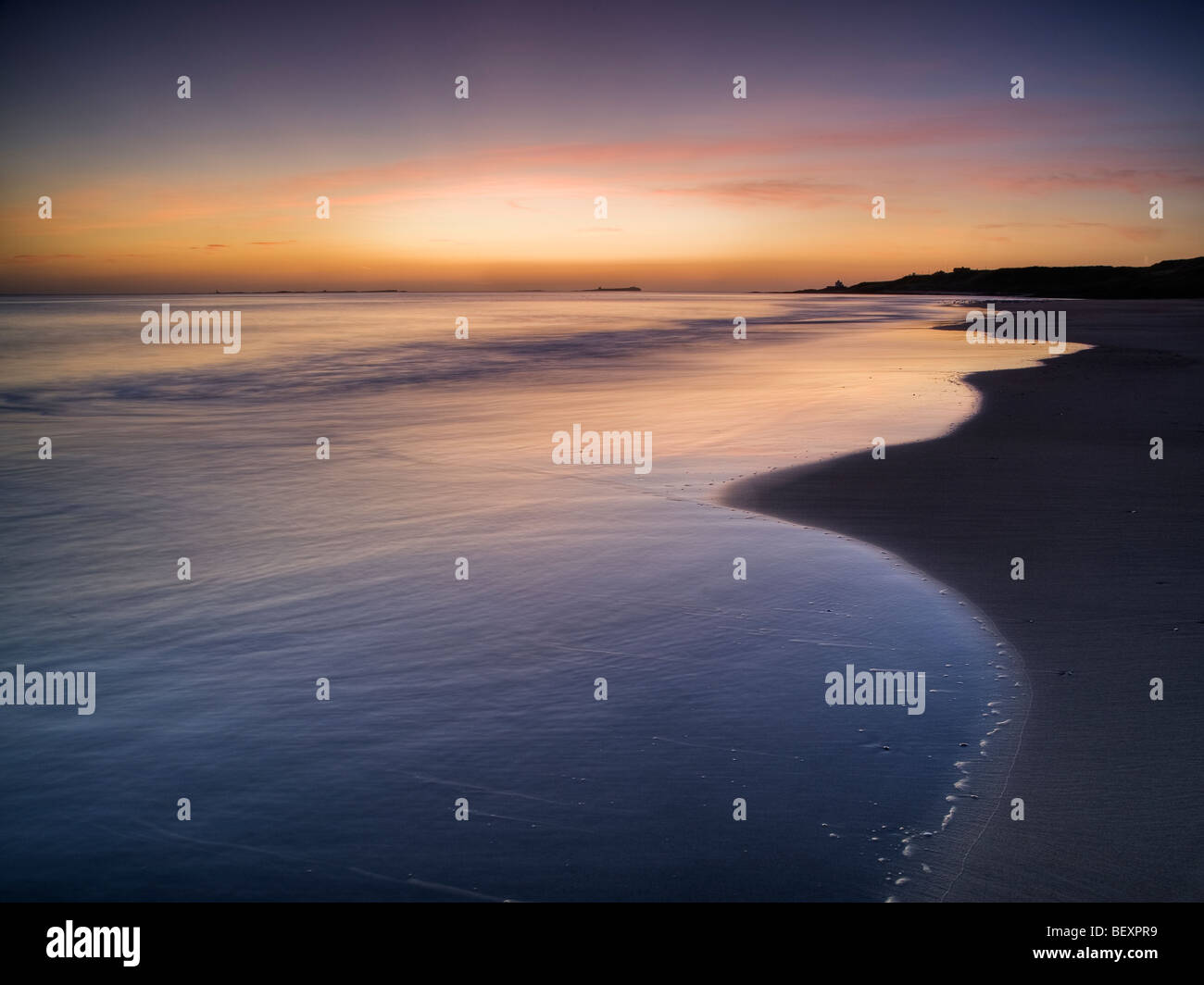 Pink pre-dawn light illuminates the sea at Budle Bay, Northumberland ...