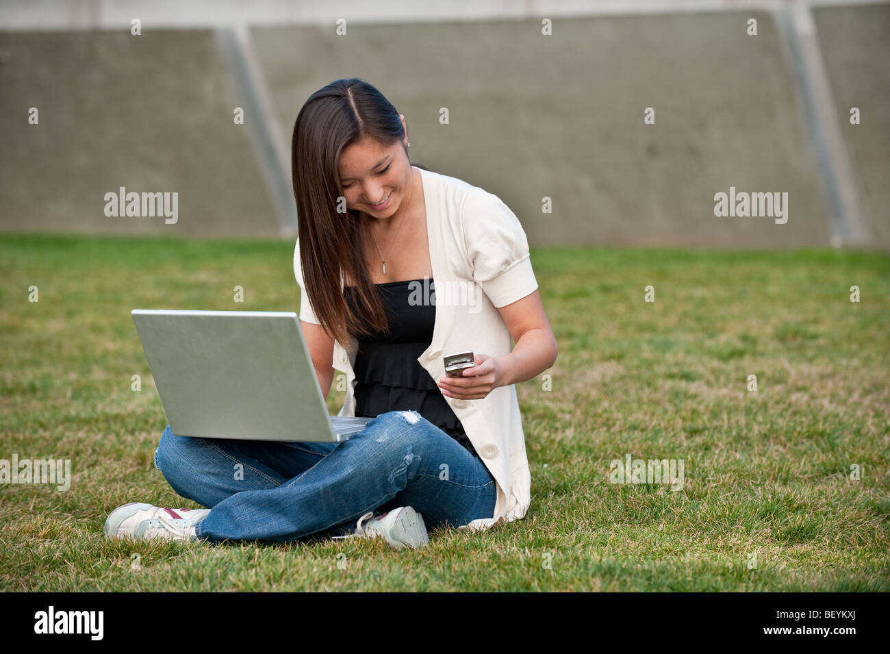 A teenage girl walking on her computer and talking to her cell phone ...