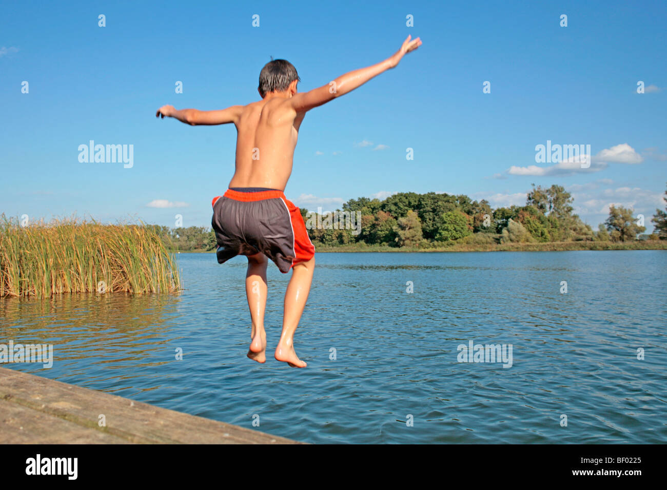 teenage boy jauntily jumping into a lake Stock Photo - Alamy