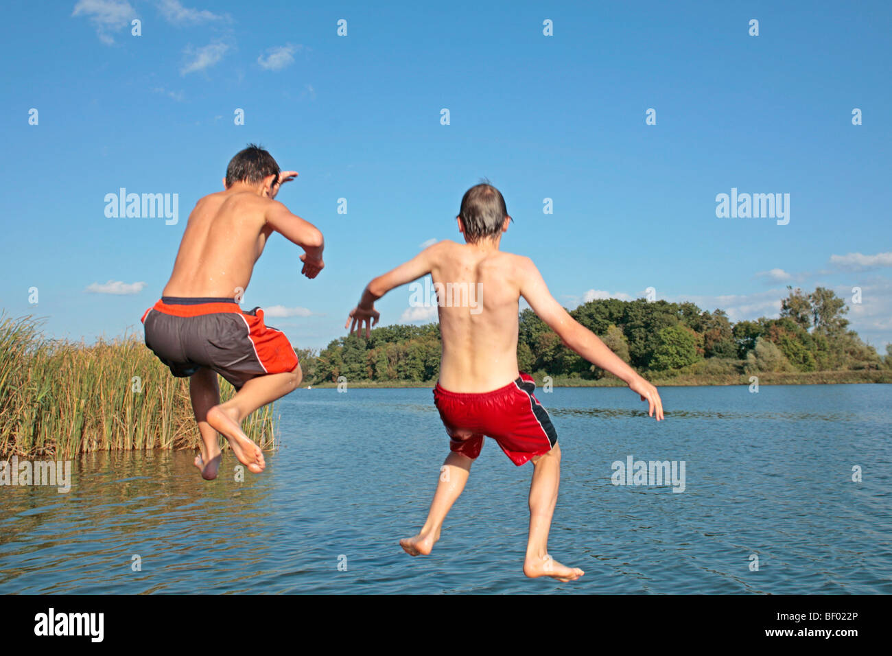 two teenage boys jauntily jumping into a lake Stock Photo - Alamy