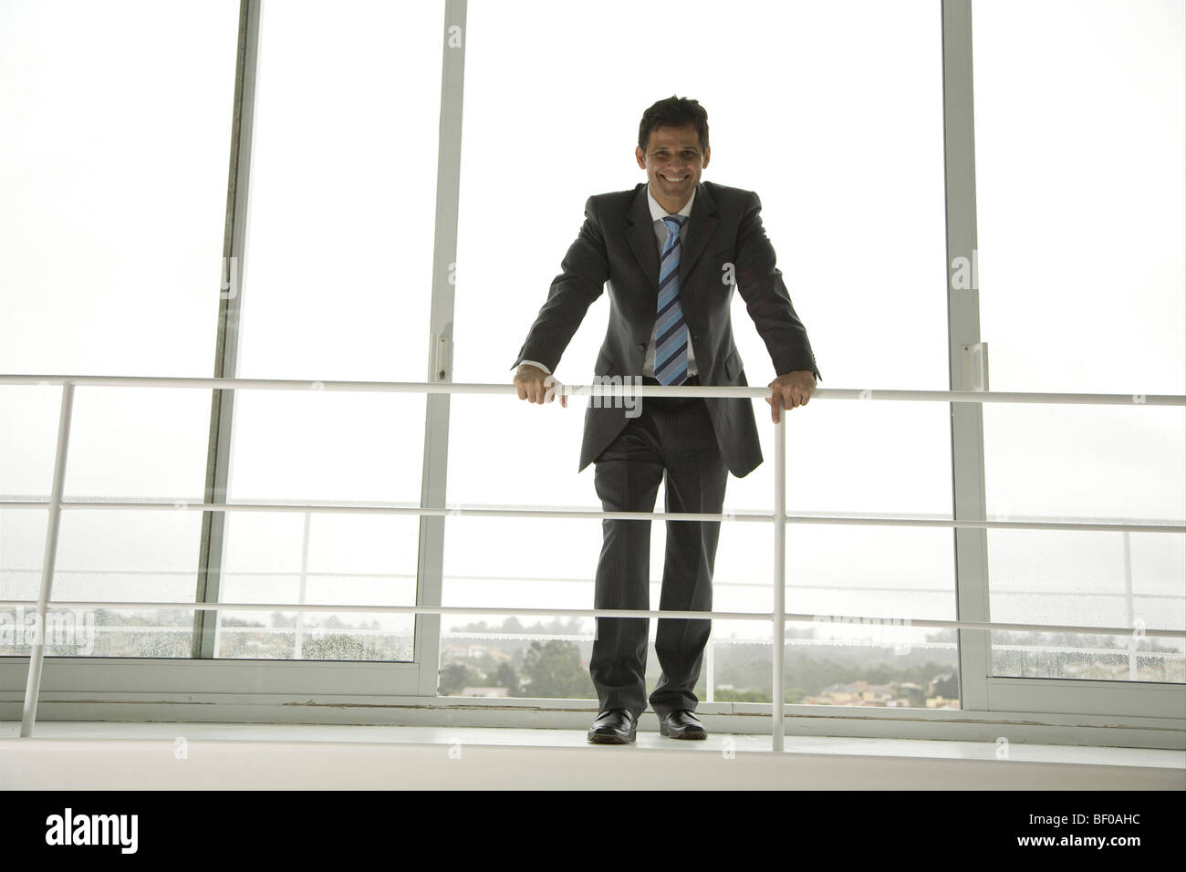 Businessman leaning against a railing and smiling Stock Photo - Alamy