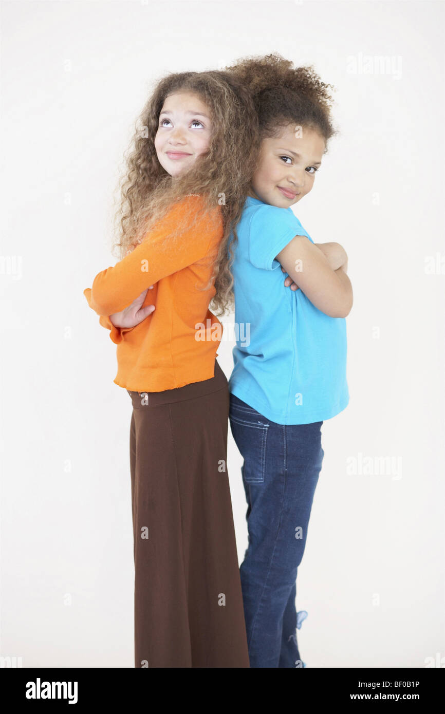 Side profile of two girls standing back to back with their arms crossed ...