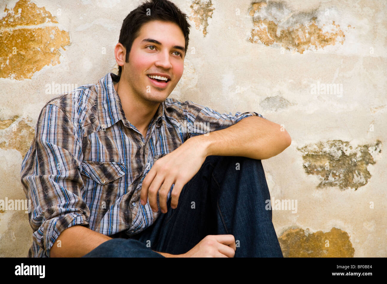 Man sitting against a wall and smiling Stock Photo - Alamy
