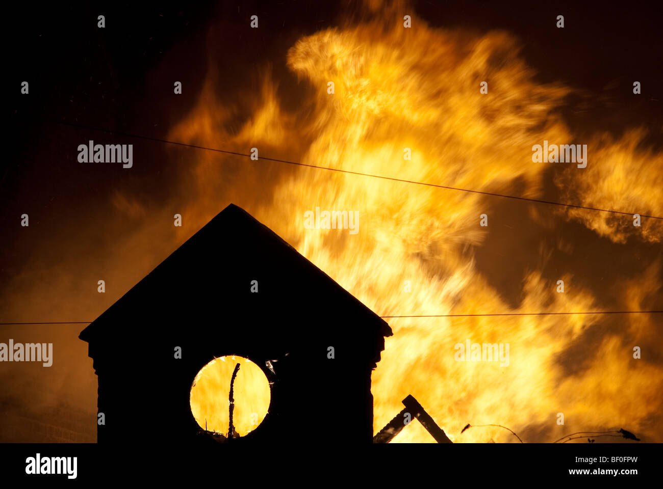 Apex of factory building on fire at night with flames in background ...