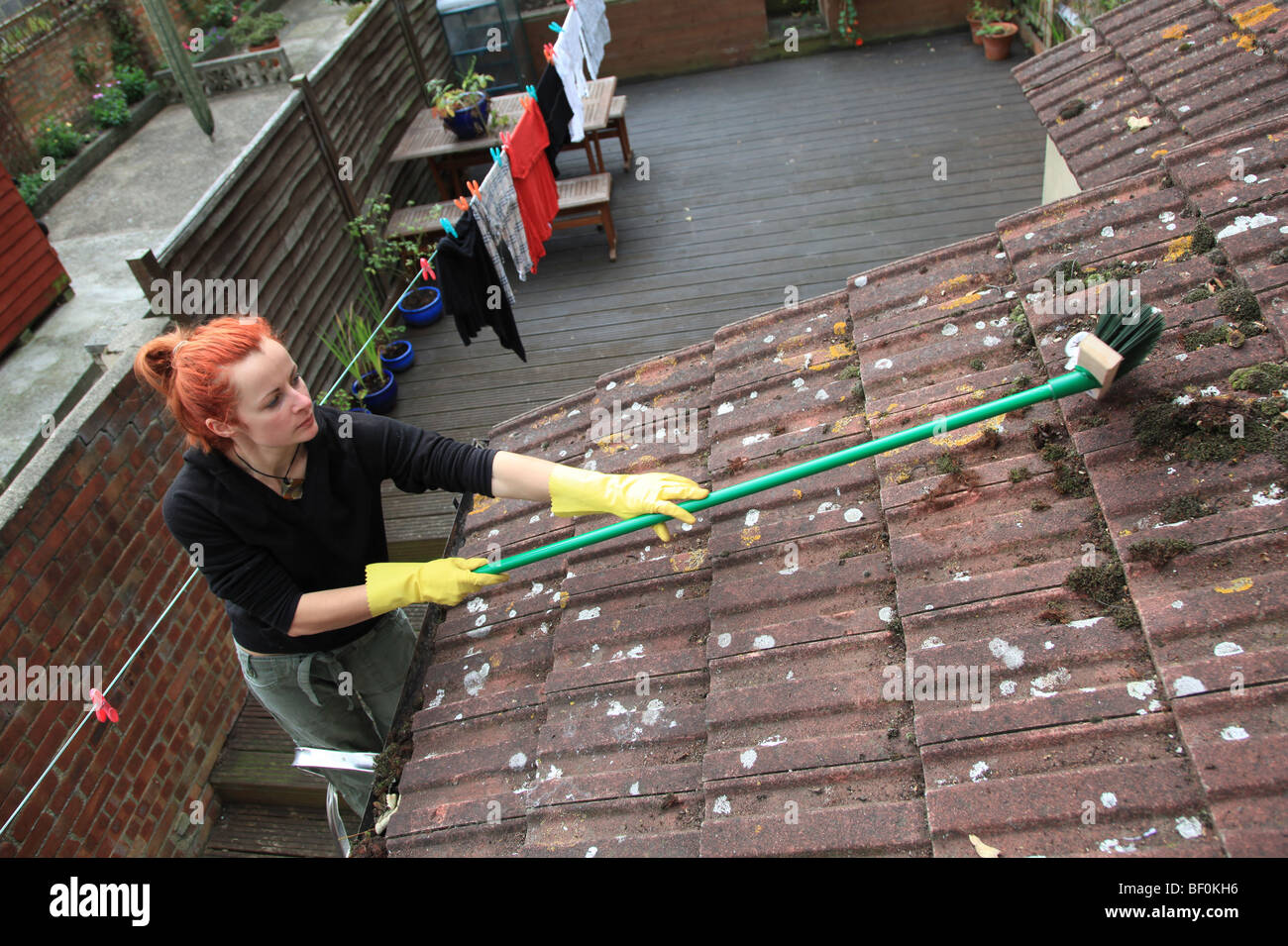 Woman clearing leaves and moss from roof and gutters Stock Photo - Alamy