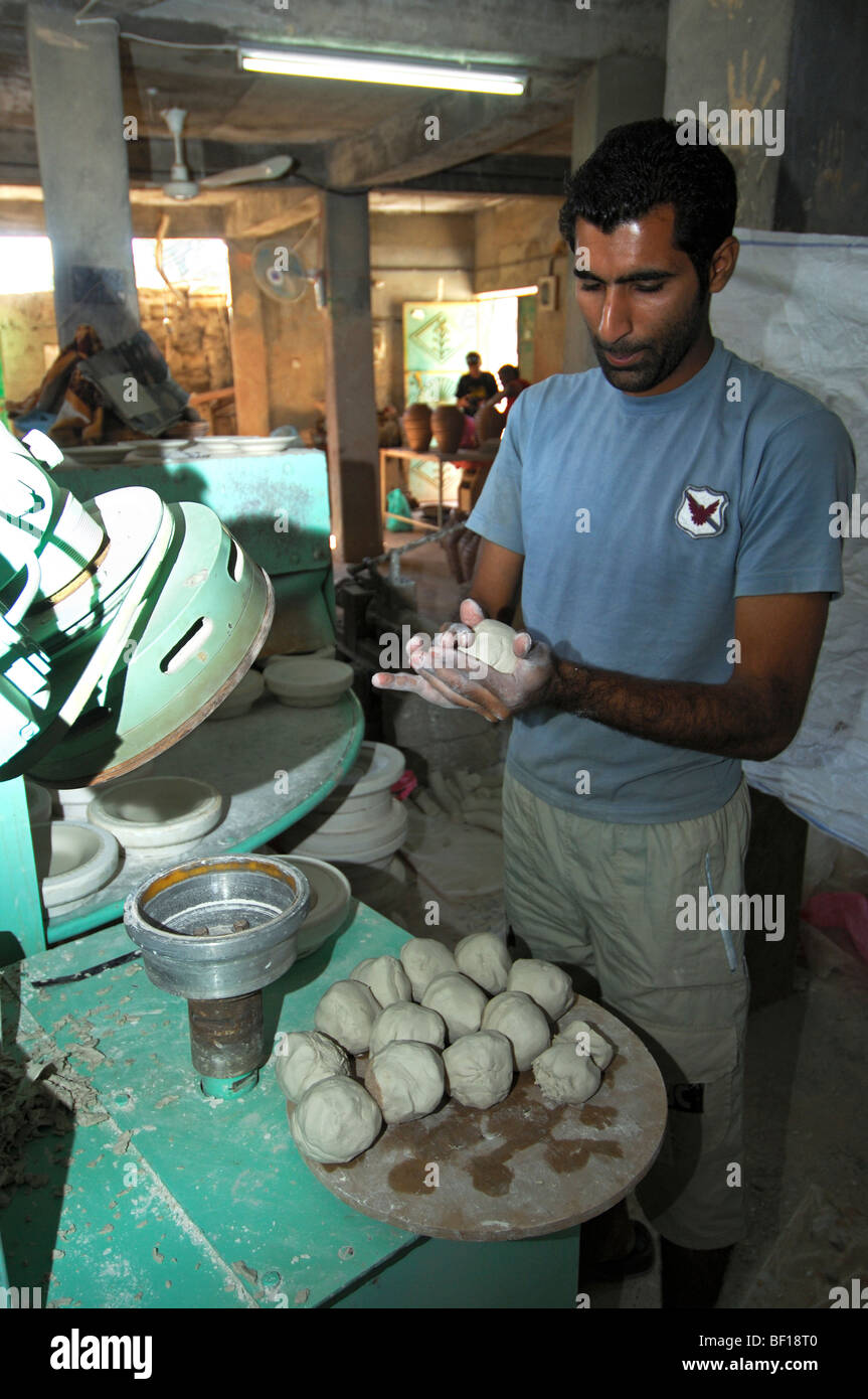 Potter forming chunks of clay for processing on a mechanical potter's ...