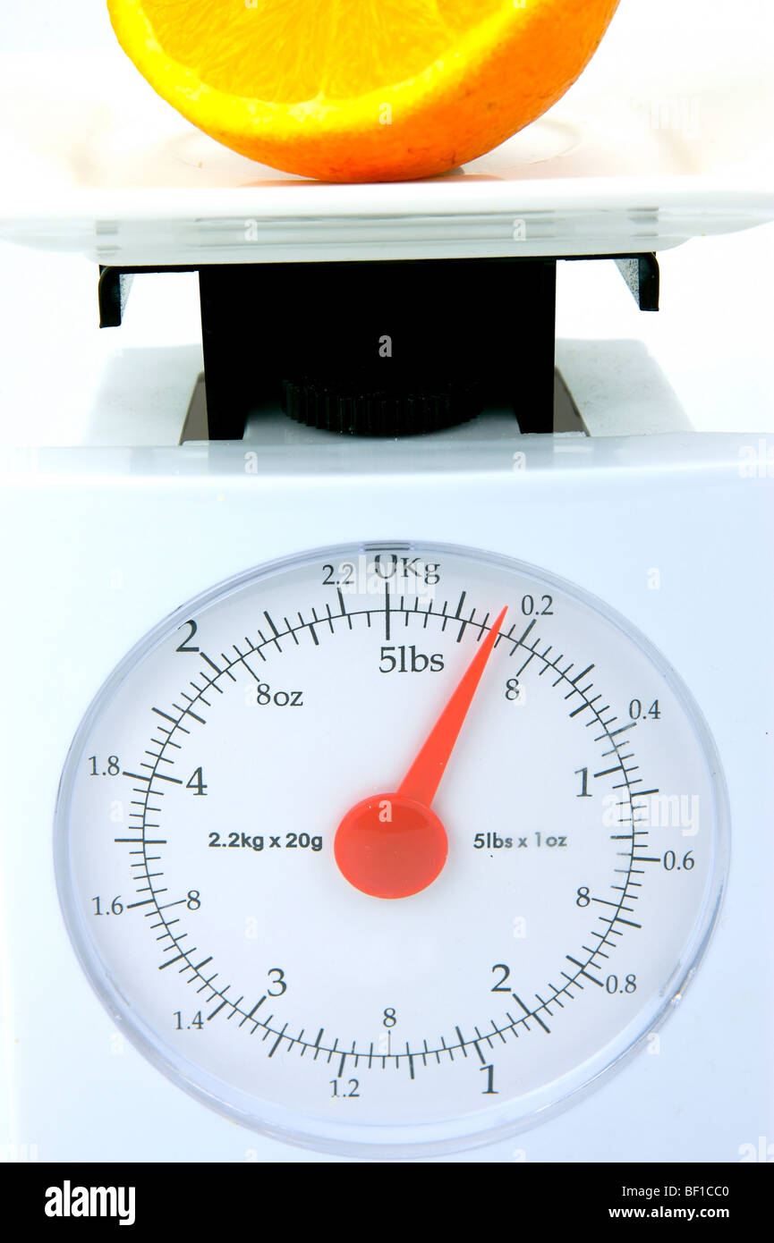A sliced orange on top of a set of kitchen scales isolated against a ...