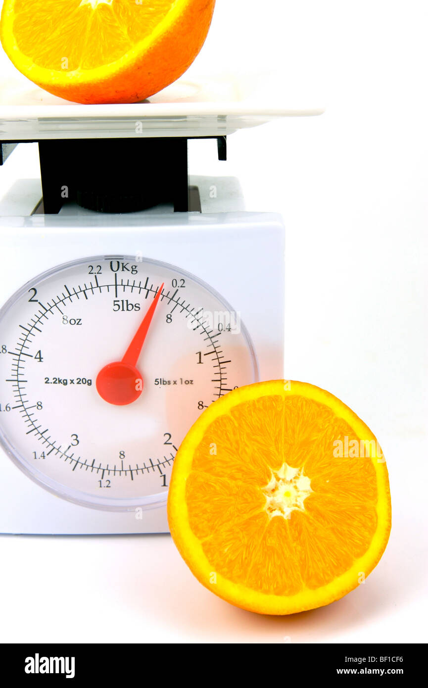 A sliced orange on top of a set of kitchen scales isolated against a ...