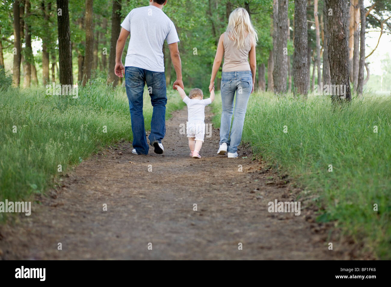 Two parents walking along a forest path with their young daughter Stock ...