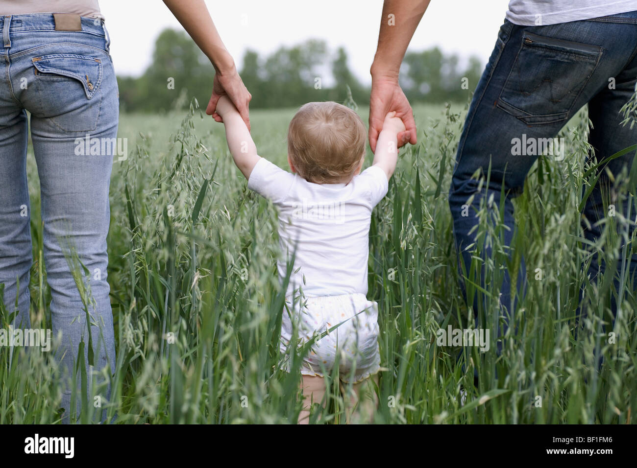 Two parents teaching their baby daughter to walk Stock Photo - Alamy