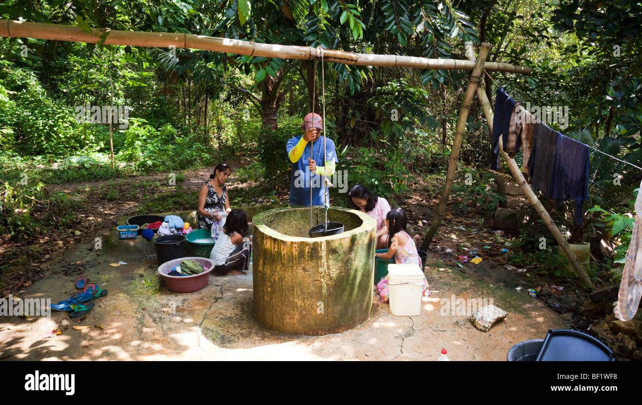 A Filipino man drawing water from a well whilst women and children wash ...