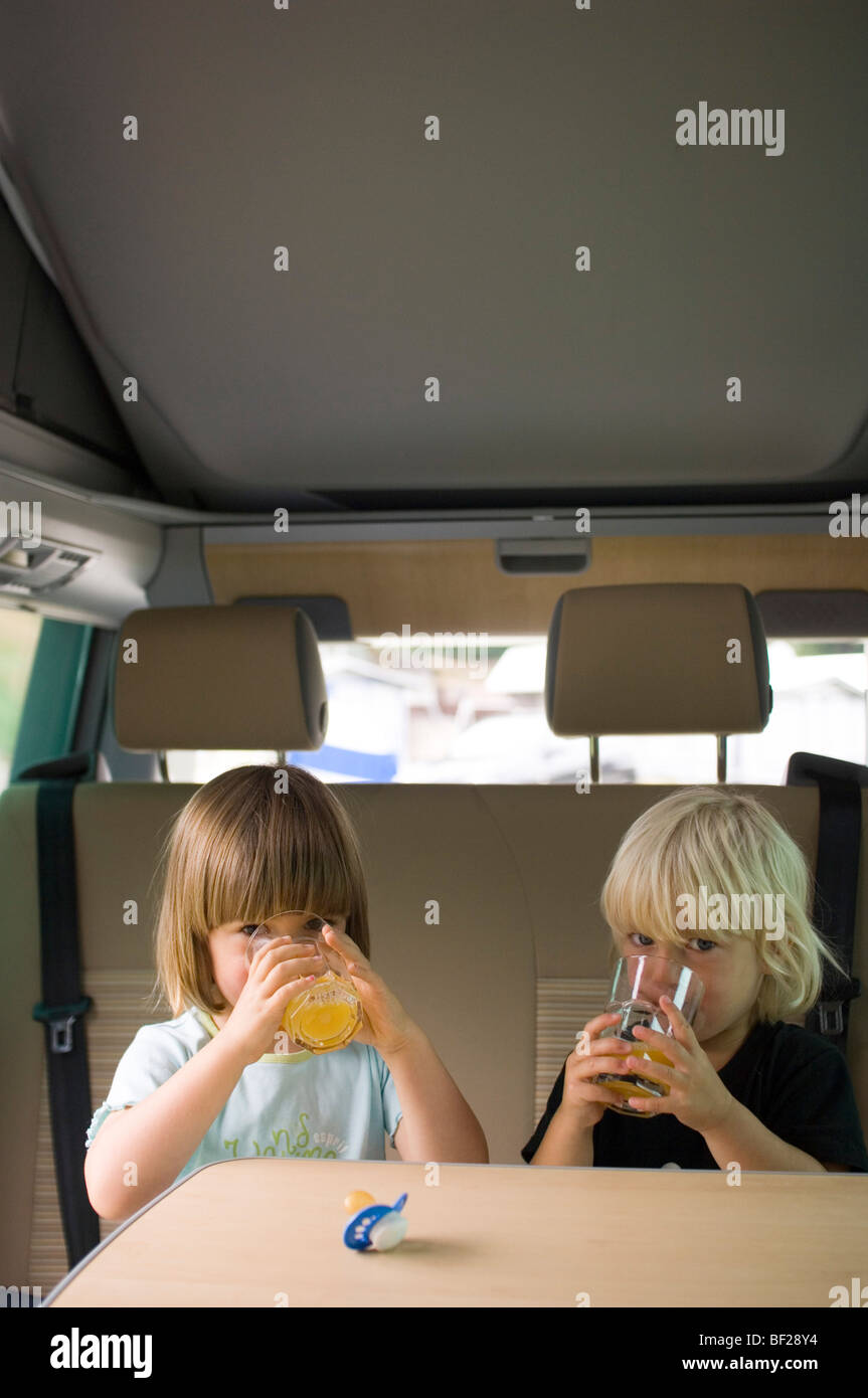 Two children sitting in a camper bus drinking orange juice, Bavaria ...
