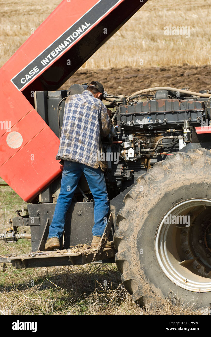 A farmer performs maintenance on a tractor in the field during planting ...