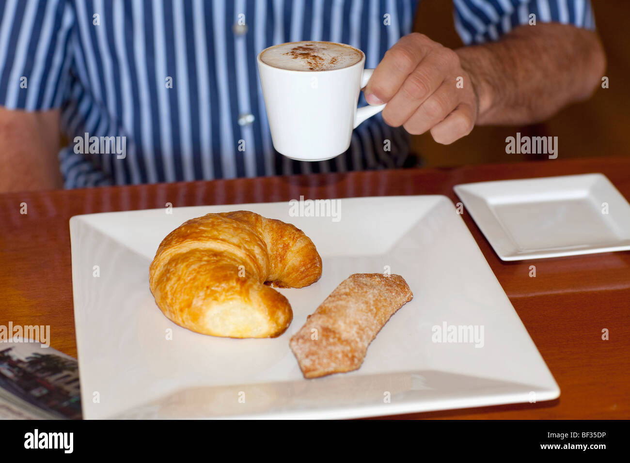 Mid section view of a man drinking coffee with a croissant and cracker ...