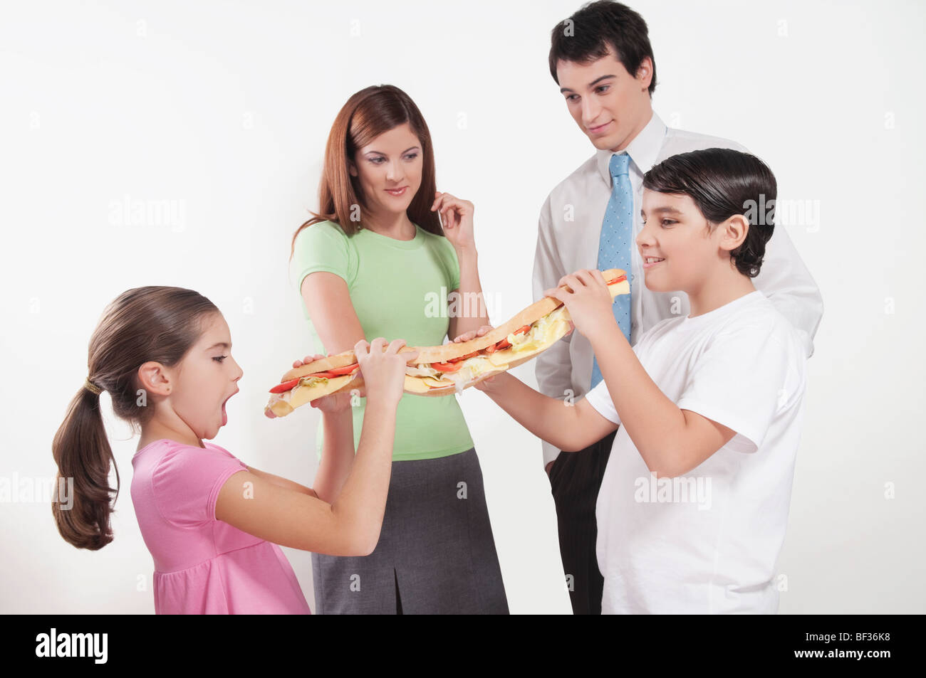 Two children eating a submarine sandwich in front of their parents ...