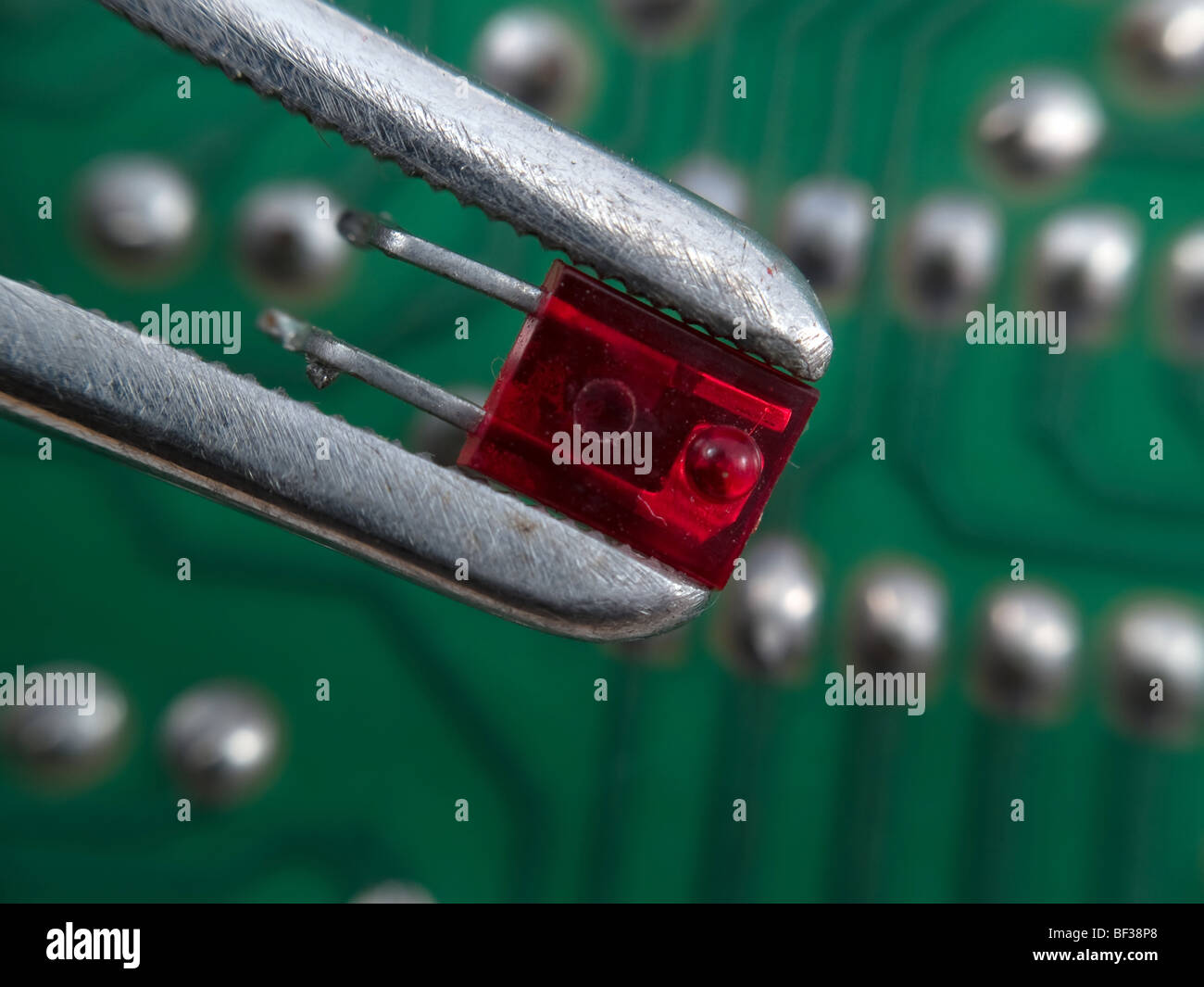 Red LED in pincers elctronic assembly macro Stock Photo - Alamy