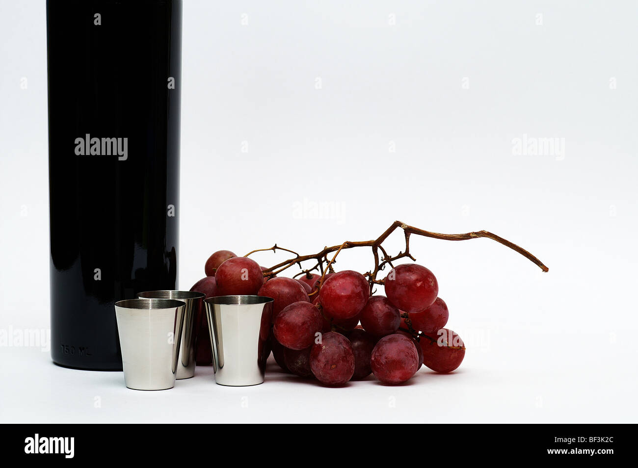 Three steel cups in front of banch of red grapes and a part of red wine ...