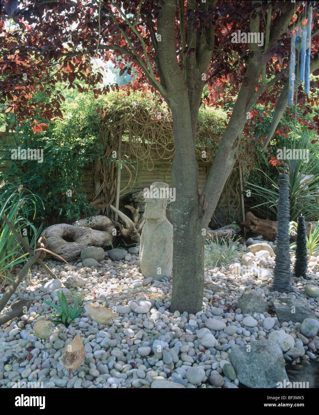 Stone primitive sculpture and seashore pebbles below tree with wind ...