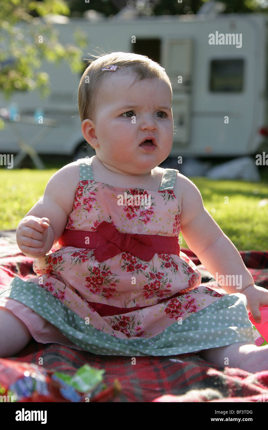 Portrait of a contented looking one year old baby girl sitting on a rug ...